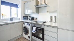 Cozinha moderna com máquina de lavar, forno, micro-ondas e janela com persiana azul.