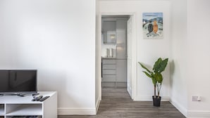 Uma sala de estar moderna com televisão de tela plana, um móvel de entretenimento branco e um vaso com planta.