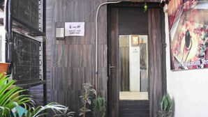 Entrada de edifício com aviso para higienizar as mãos, plantas em vasos e um cartaz na parede.