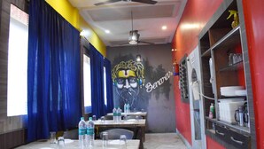 Interior de restaurante com mesas preparadas para refeições, um mural na parede e um balcão com pratos e acompanhamentos.