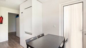 Quarto com uma mesa de jantar e cadeiras, um guarda-roupa branco, uma porta com puxador e um extintor de incêndio na parede.