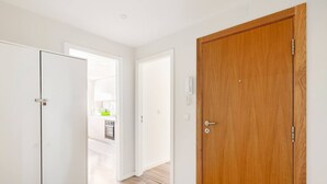 Um corredor com uma porta de madeira, uma porta branca e vista para uma cozinha.