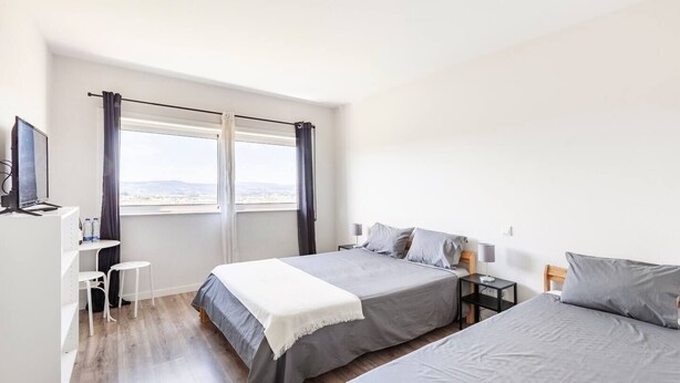 Quarto de hotel moderno com duas camas, uma escrivaninha e uma televisão.