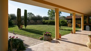 Uma varanda coberta com vista para um jardim e gramado bem cuidados.