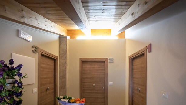 Um corredor com portas de madeira, uma porta branca com o número 3 e uma tigela de frutas sobre uma mesa.