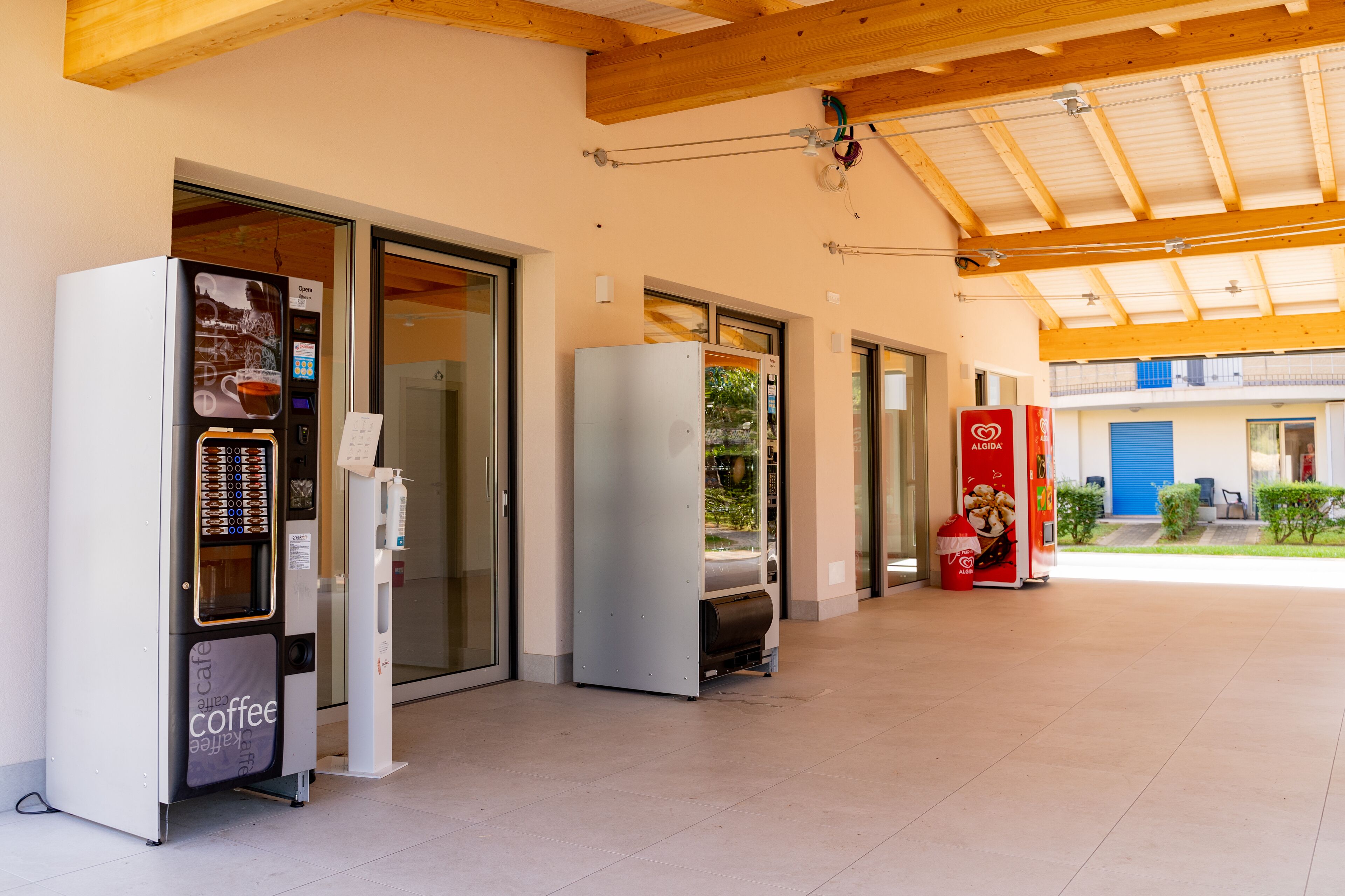 Espaço interno moderno com máquina de café, uma geladeira branca grande e uma máquina de Coca-Cola vermelha.