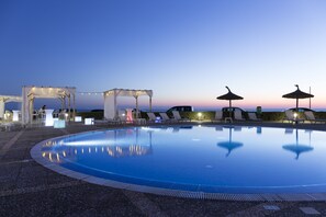 Piscina com espreguiçadeiras e guarda-sóis, rodeada por uma área coberta com iluminação de luzes de corda.