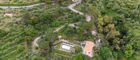 Vista aérea de uma propriedade com piscina, jardim e estrada sinuosa.