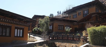 Um edifício tradicional com uma ponte de pedra, rodeado por vegetação e outras construções semelhantes.