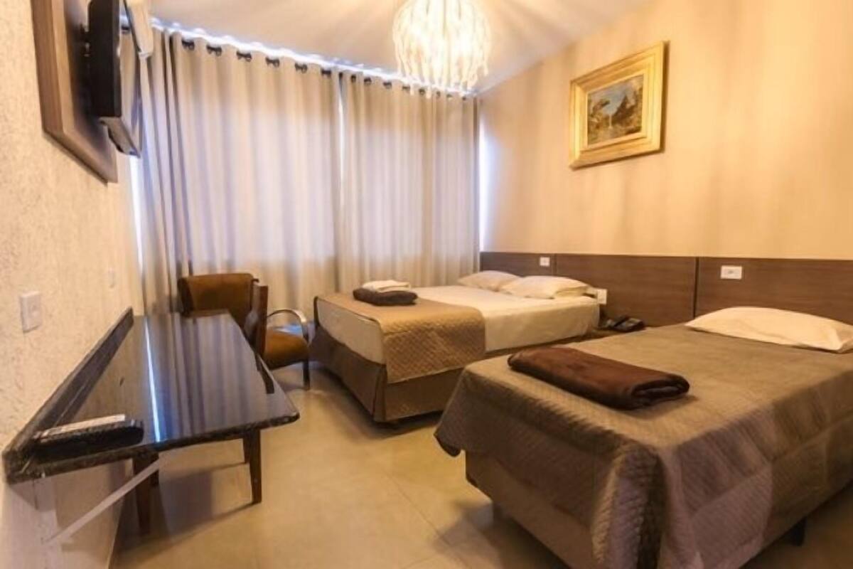 Quarto de hotel com duas camas, uma escrivaninha, uma cadeira e uma televisão.