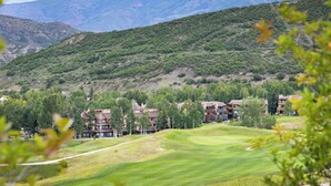 Um campo de golfe com vista para uma paisagem montanhosa e um conjunto de edifícios altos ao fundo.
