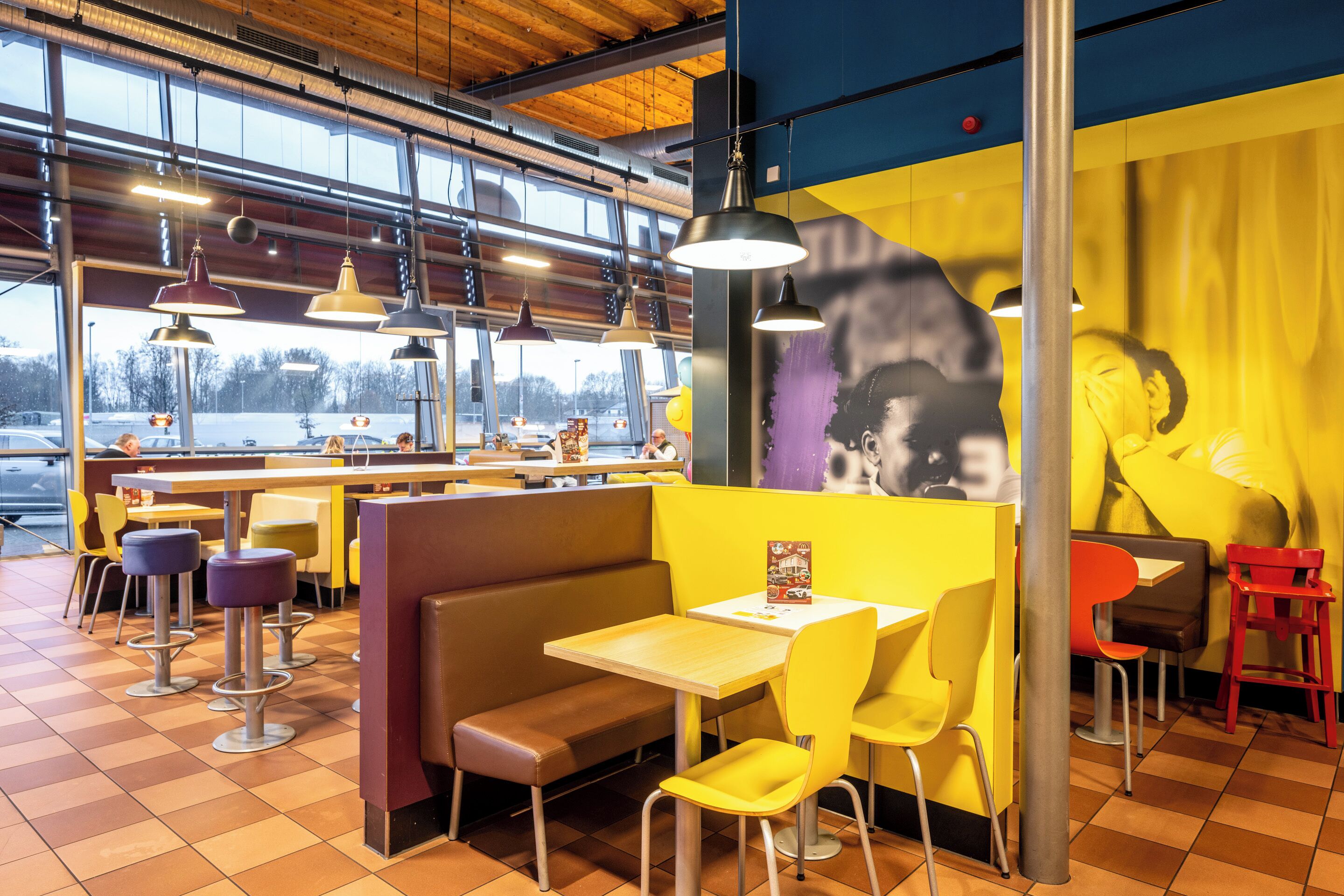 Interior de restaurante com cabines, mesas altas e cadeiras amarelas.