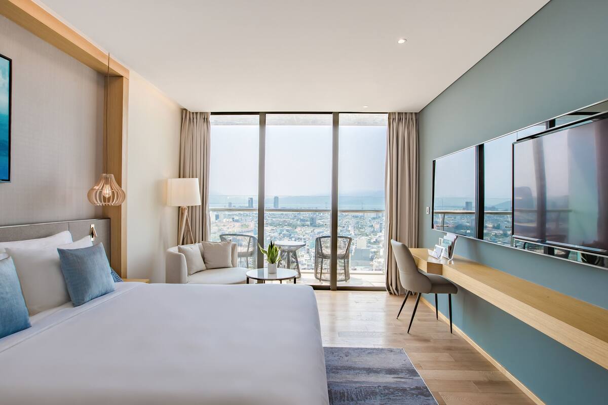 Quarto de hotel moderno com uma cama grande, uma mesa de escritório e uma televisão.