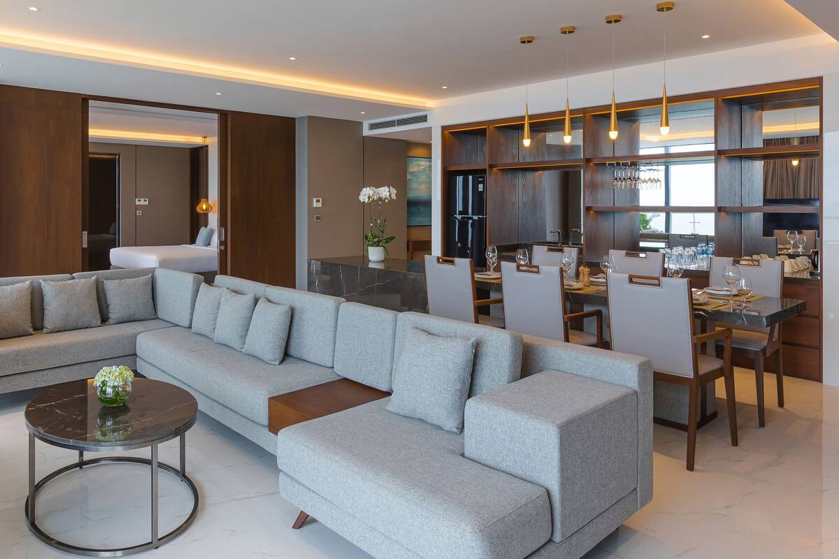 Uma sala de estar moderna com um sofá modular cinzento, uma mesa de centro redonda e um espaço de jantar com uma mesa de mármore e cadeiras.