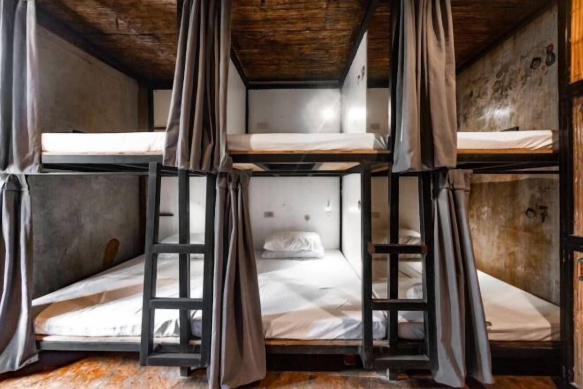 Quarto com beliche, vigas de madeira, cortinas e parede de concreto.