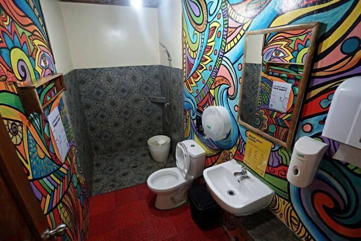 Casa de banho com murais coloridos, sanita branca, lavatório e zona de duche.