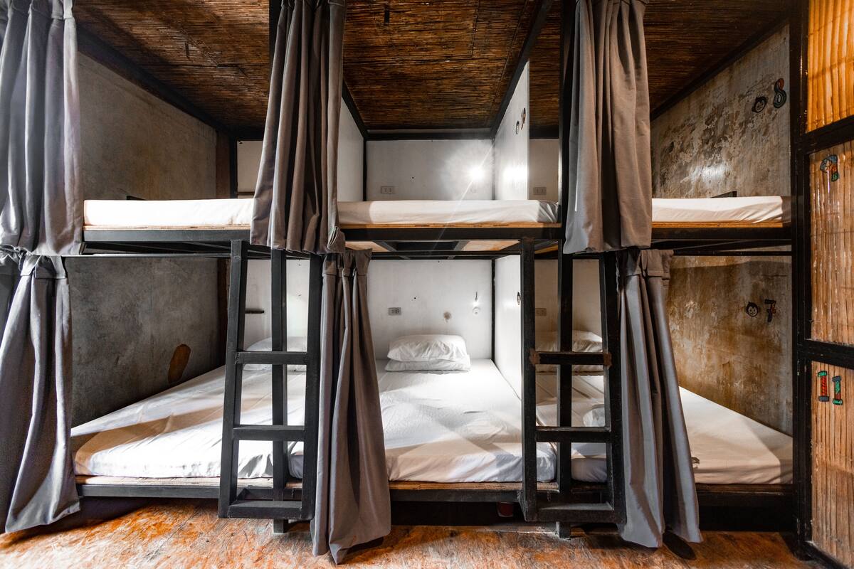 Quarto com beliches, vigas de madeira e cortinas.