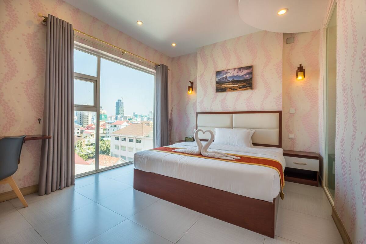 Quarto de hotel com cama grande, vista da cidade e escrivaninha com cadeira.