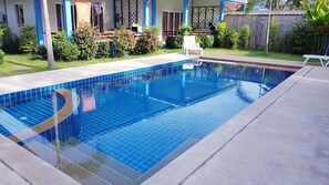 Piscina com azulejos azuis, rodeada por um terraço coberto com mobiliário de exterior.