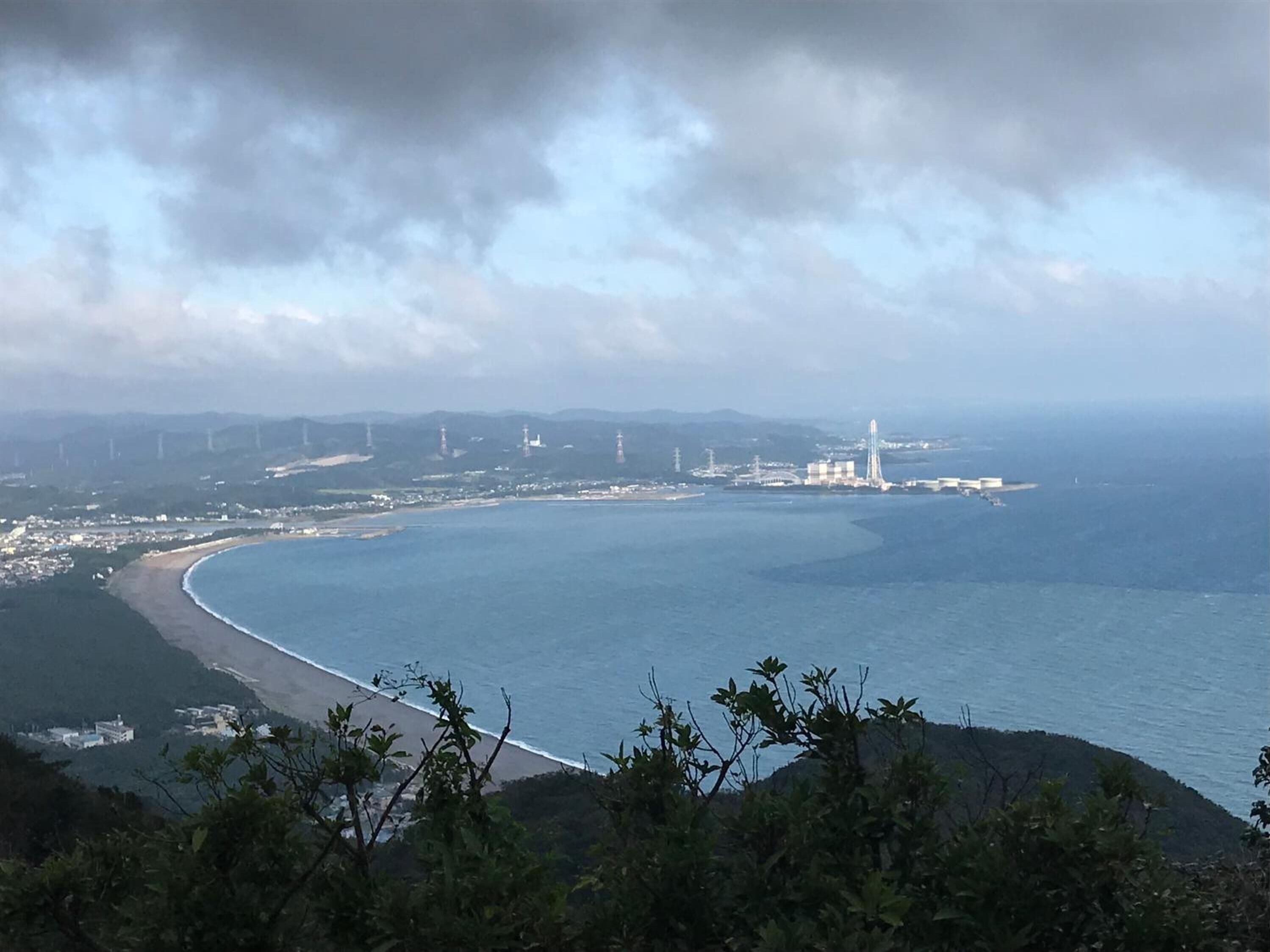 Paisagem costeira com praia, oceano e edifícios ao longe, incluindo um farol.