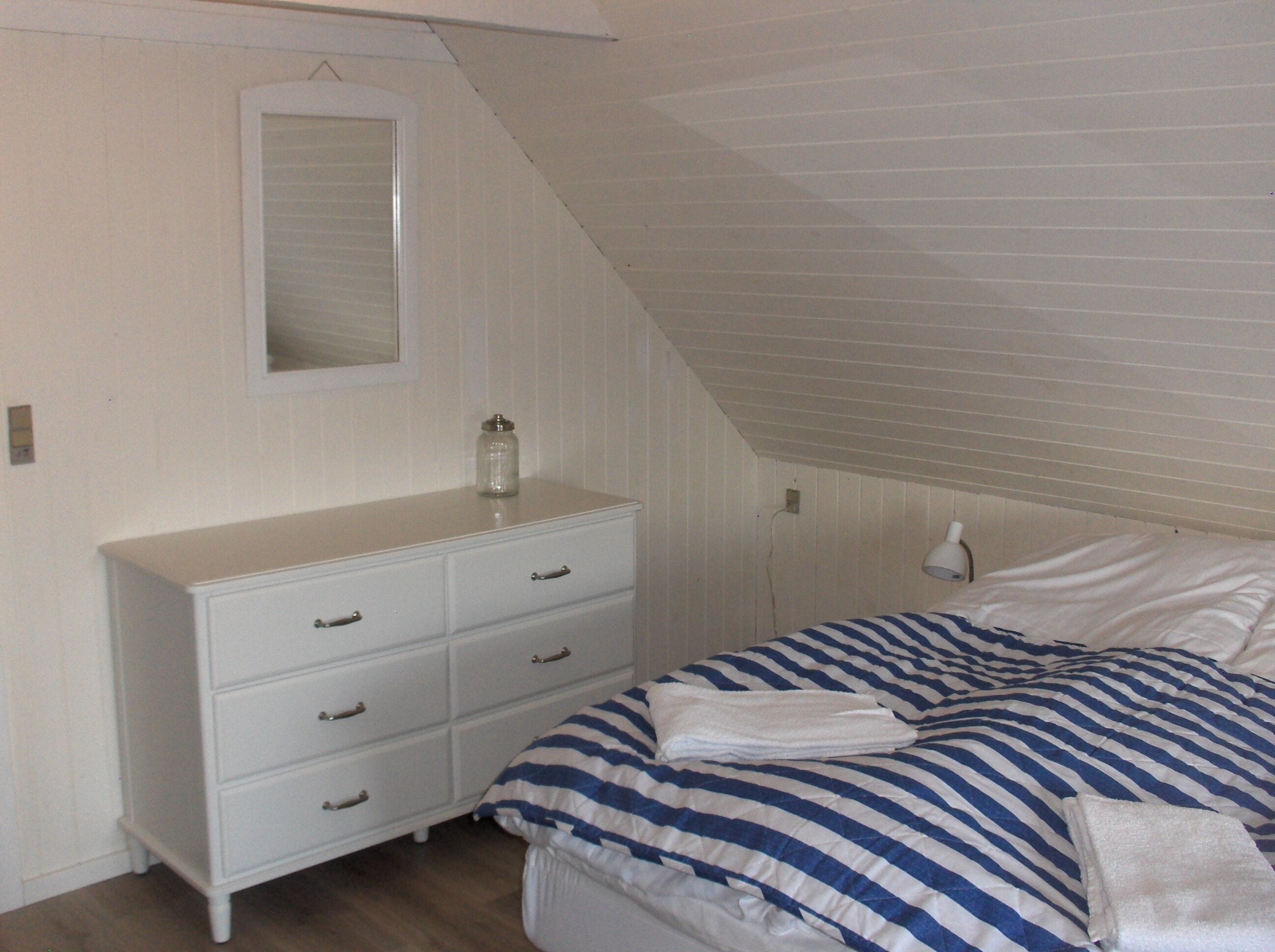 Quarto com cama, cômoda, espelho e abajur.