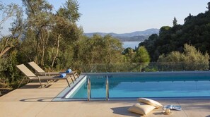 Piscina com espreguiçadeiras e vista para um lago e colinas.
