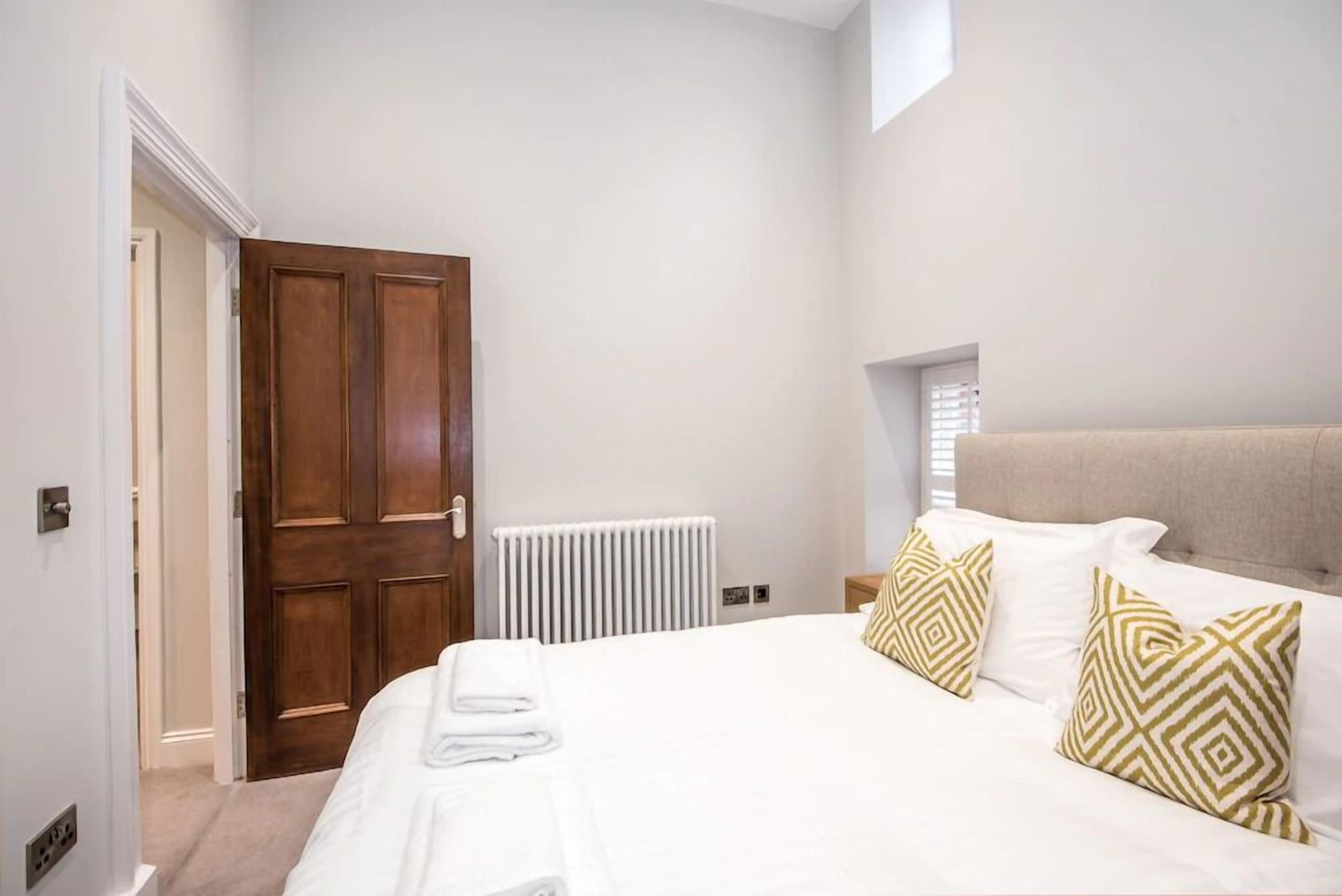 Quarto com cama grande, porta de madeira, radiador e janela com persianas.
