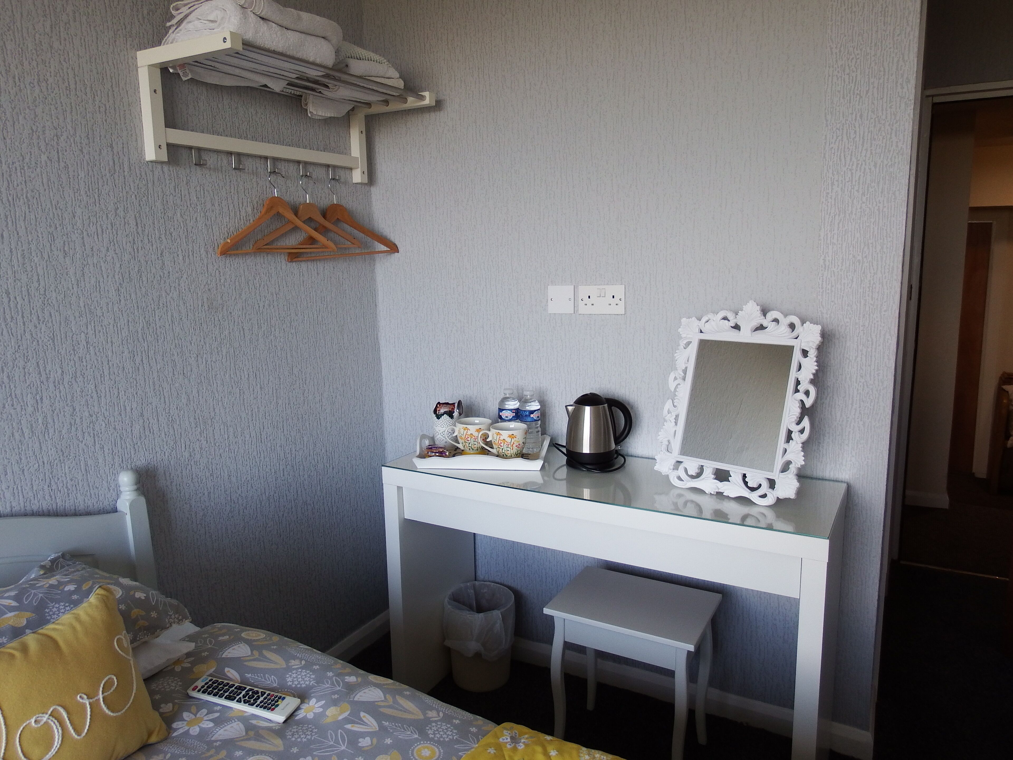Quarto com cama, escrivaninha com espelho, cabideiro e uma pequena lixeira.