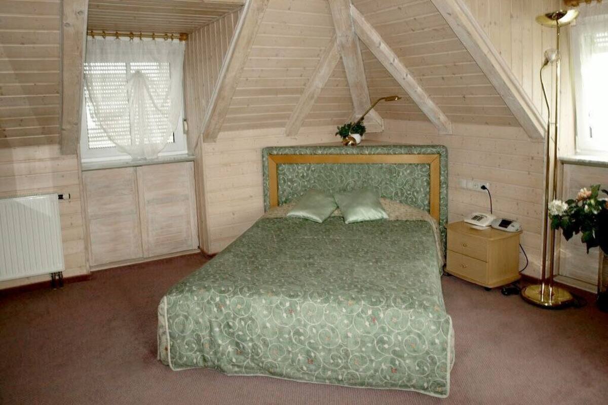 Quarto com cama, mesa de cabeceira, abajur e janela com cortinas.