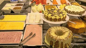 Buffet com diversos itens de comida, incluindo bolos, doces e fatias de carne.