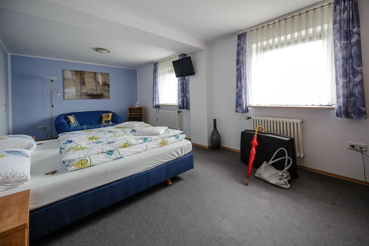 Quarto com cama, escrivaninha, cadeira, radiador, televisão e janela com cortinas.