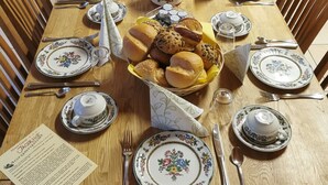 Mesa de jantar posta com louça floral, pão e um cardápio.