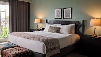 Quarto de hotel com uma cama grande, duas mesas de cabeceira, uma janela com cortinas e uma obra de arte na parede.