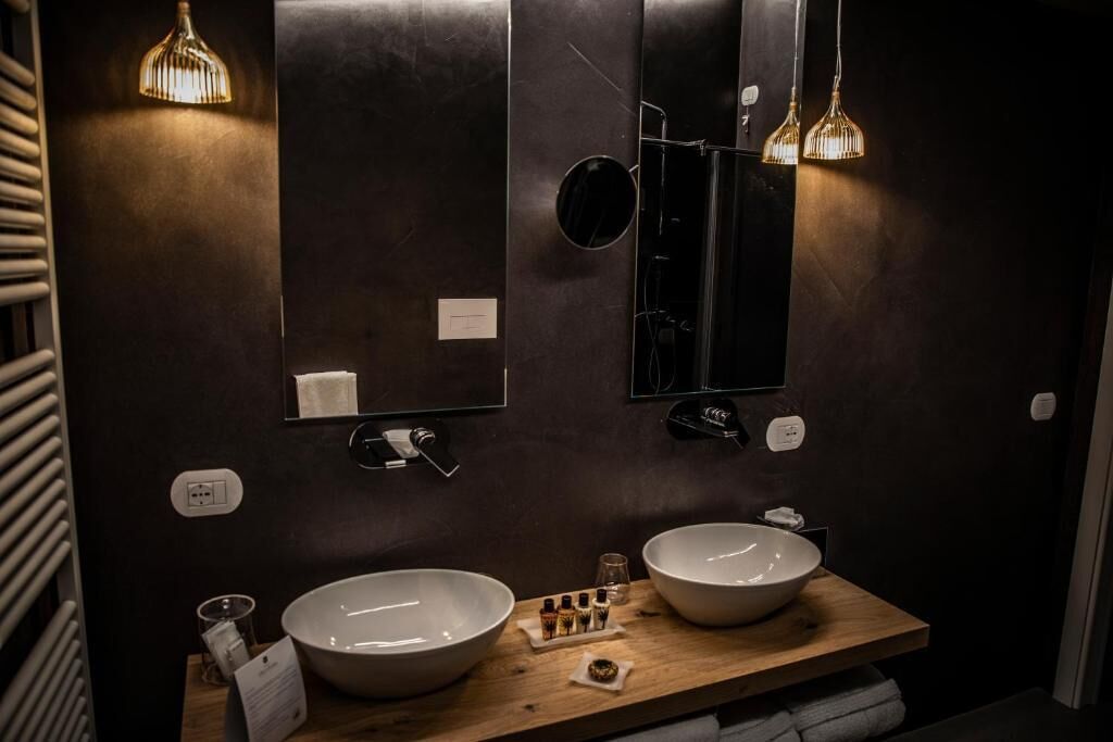 Casa de banho moderna com duas grandes pias brancas, toucador de madeira, espelho e luzes pendentes.