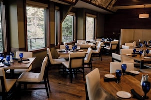 Um restaurante com várias mesas e cadeiras, janelas amplas e teto de madeira.