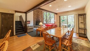 Uma ampla área de jantar com uma grande mesa de madeira e cadeiras, uma lareira e vista para o exterior.
