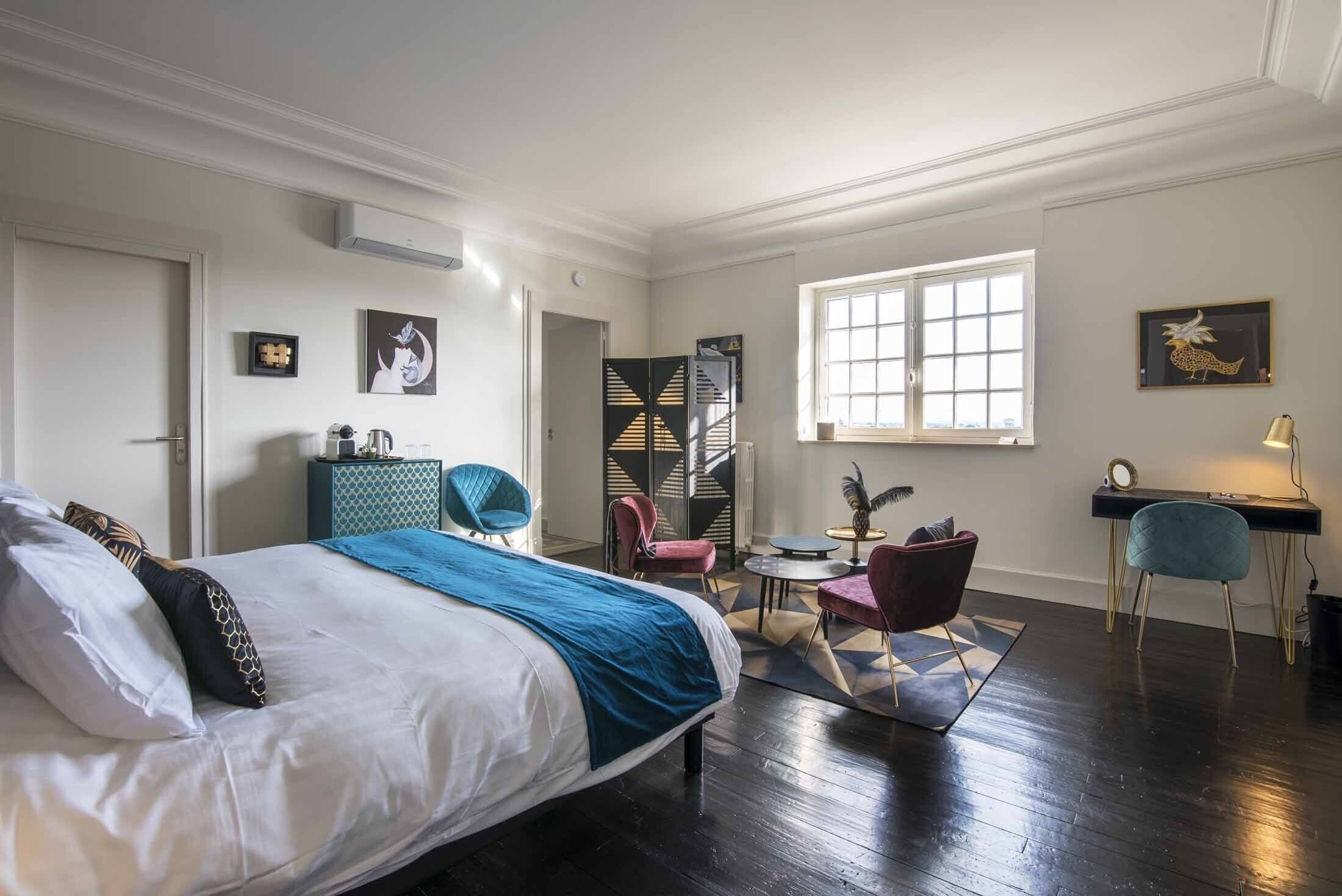 Quarto de hotel moderno com uma cama grande, uma escrivaninha, uma cadeira e uma pequena mesa.