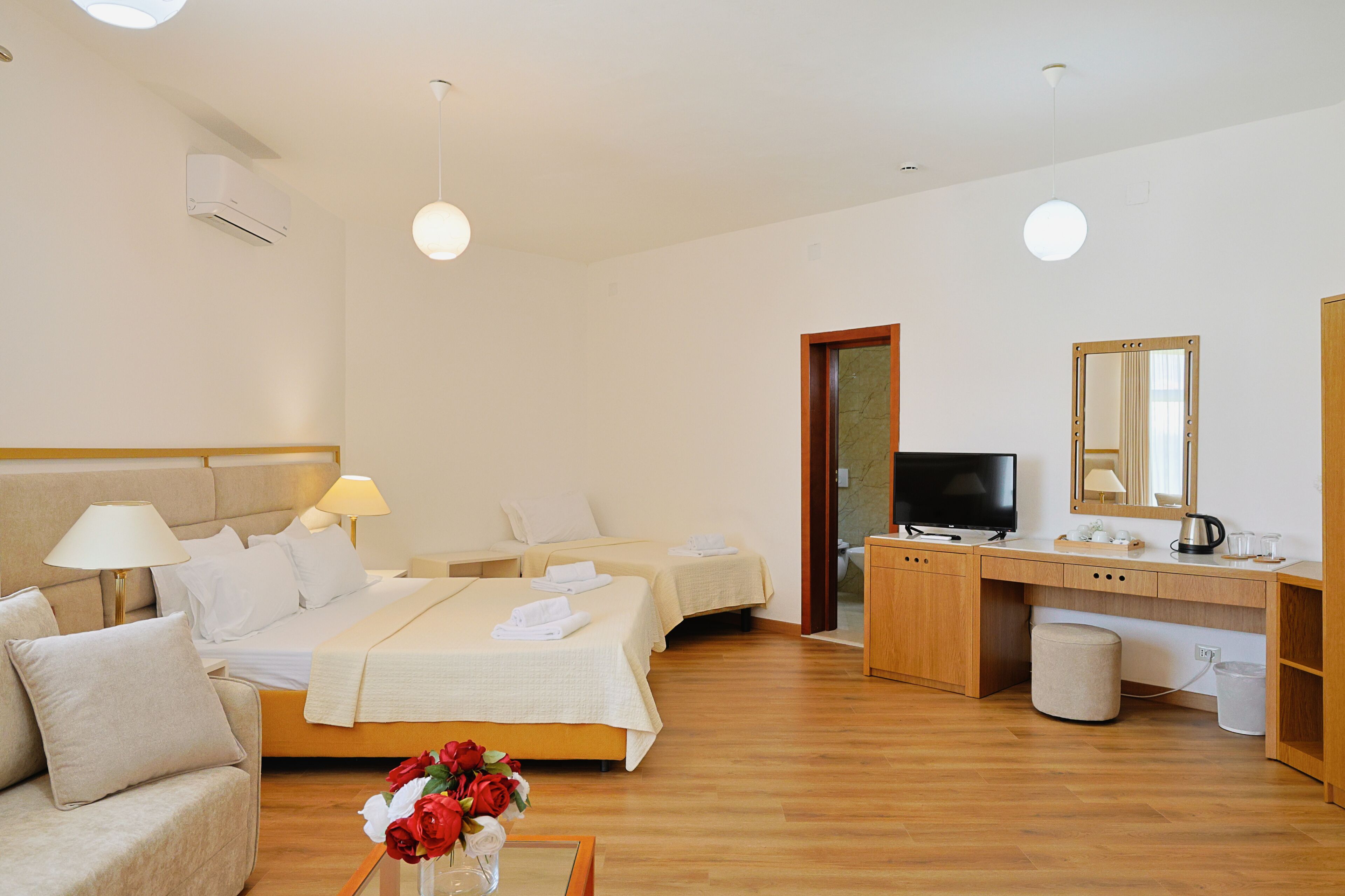 Quarto de hotel com cama, duas mesas de cabeceira com luminárias, escrivaninha com televisão, espelho e um cesto de lixo.
