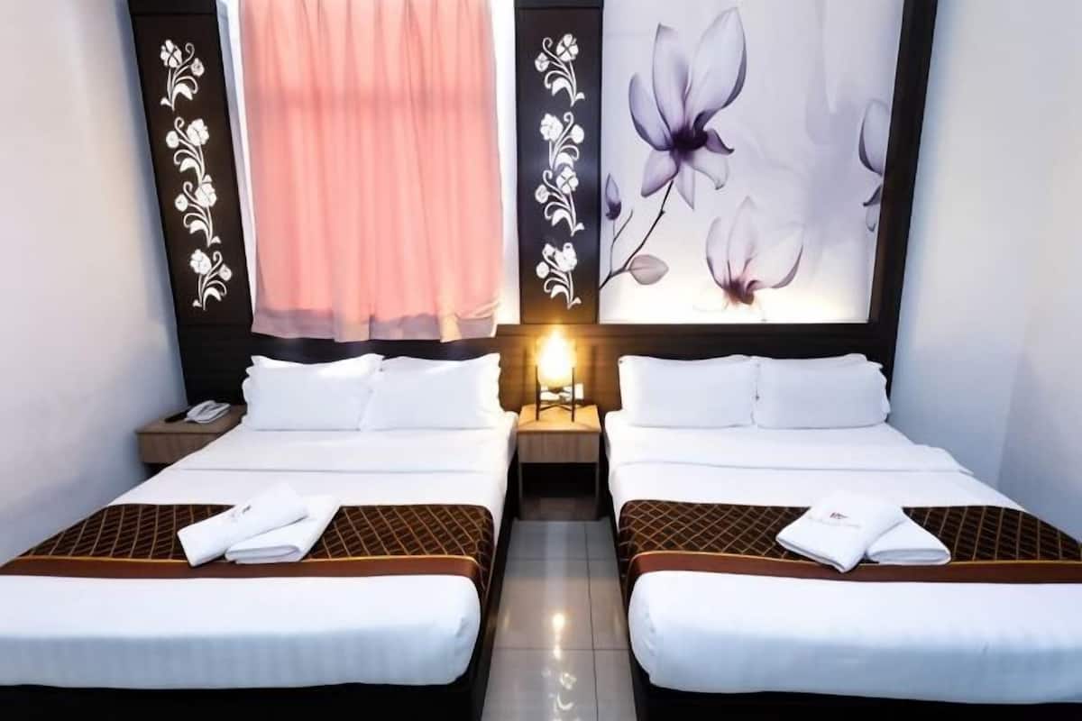 Quarto de hotel com duas camas, uma mesa de cabeceira com abajur e uma grande obra de arte floral na parede.