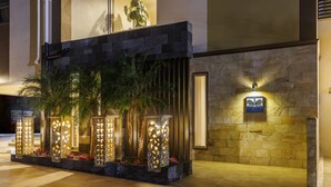 Uma entrada de hotel moderna com fachada de pedra, iluminação decorativa e uma placa indicando o nome do hotel.