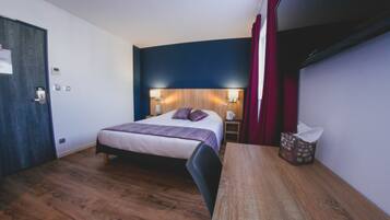 Quarto de hotel com cama, mesa de cabeceira e piso de madeira.