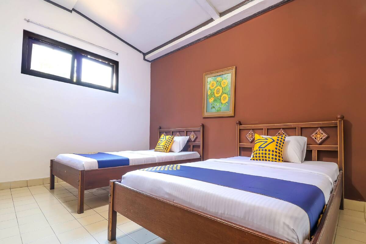 Quarto de hotel com duas camas de madeira, um quadro de girassóis e uma janela.