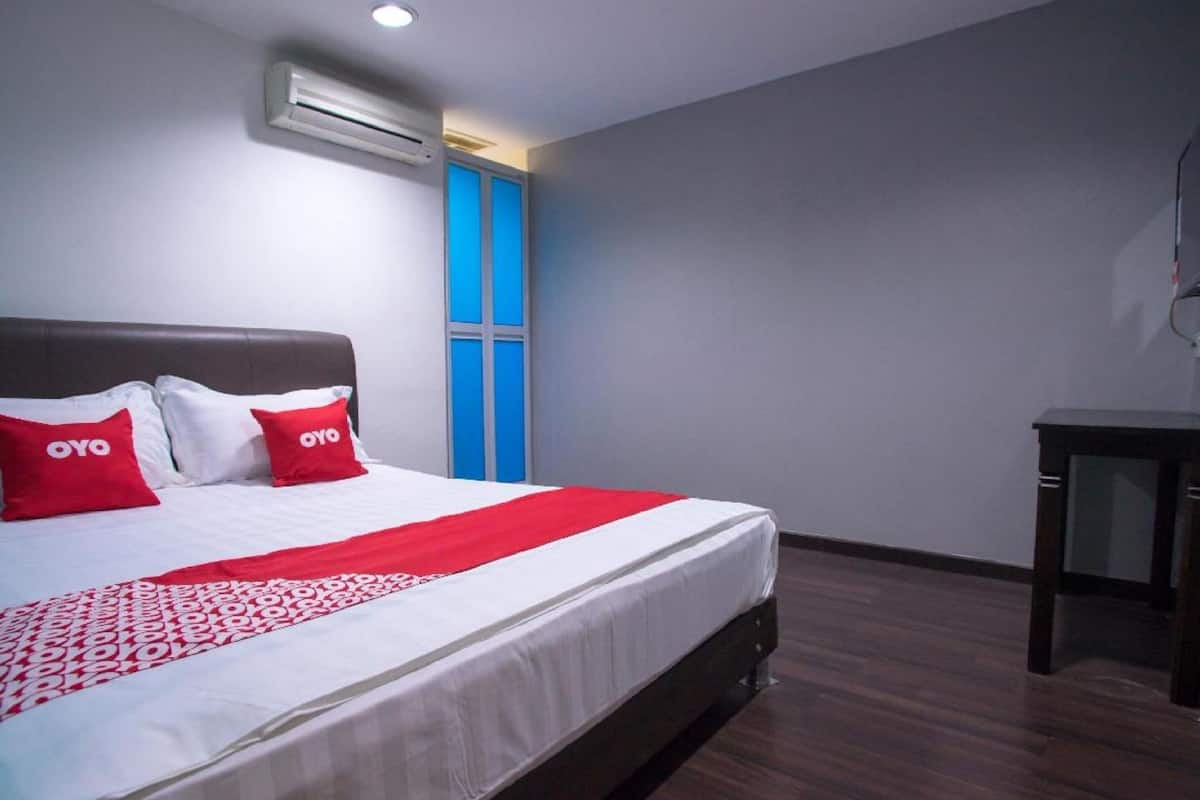 Quarto de hotel com uma cama, uma mesa de cabeceira, uma janela com moldura azul e um ar condicionado.