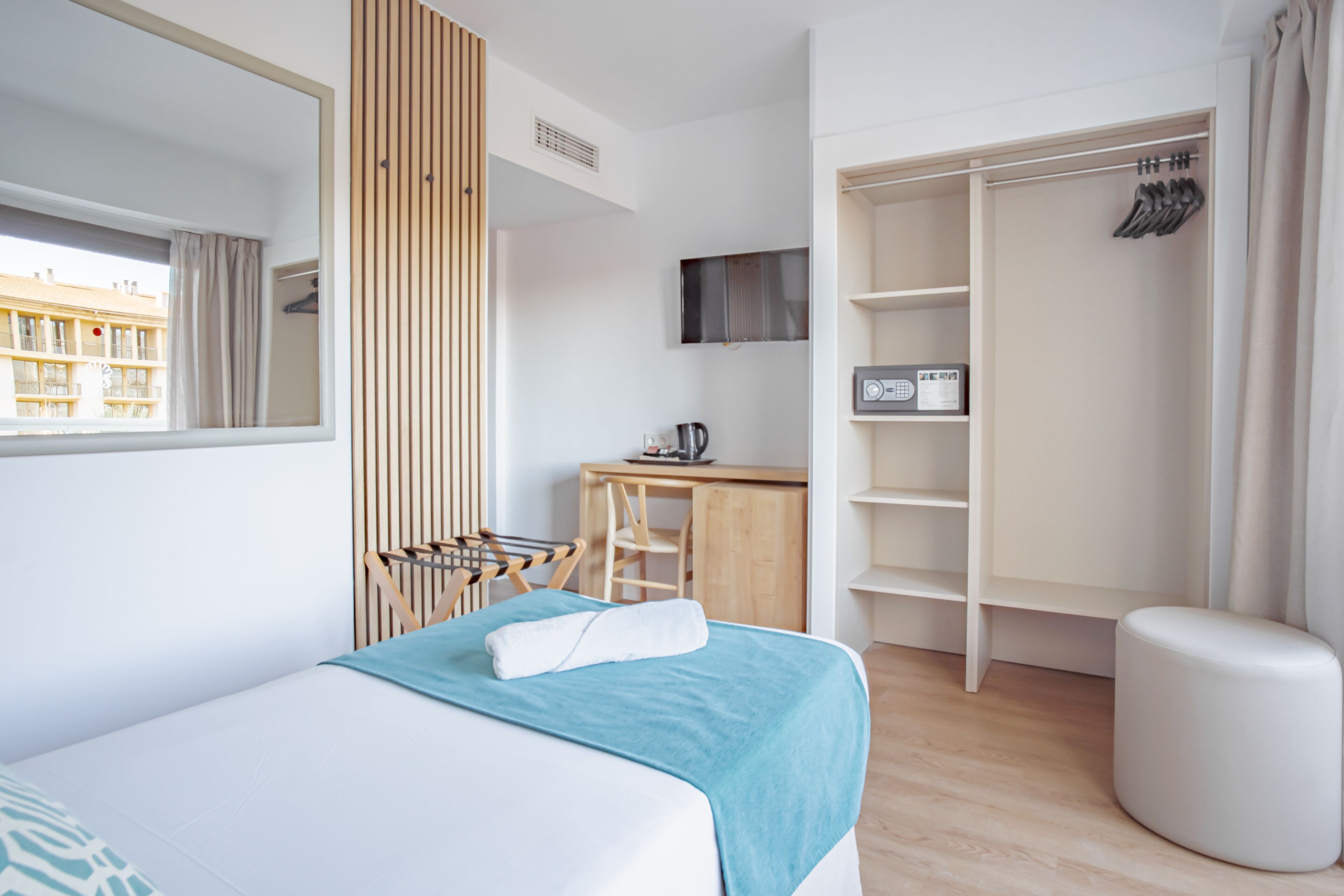 Quarto de hotel moderno com cama, escrivaninha, guarda-roupa e vista para a cidade.