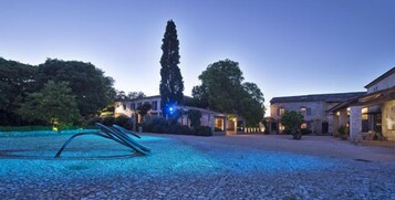 Pátio com piscina, caminho de pedra e edifícios com iluminação quente.