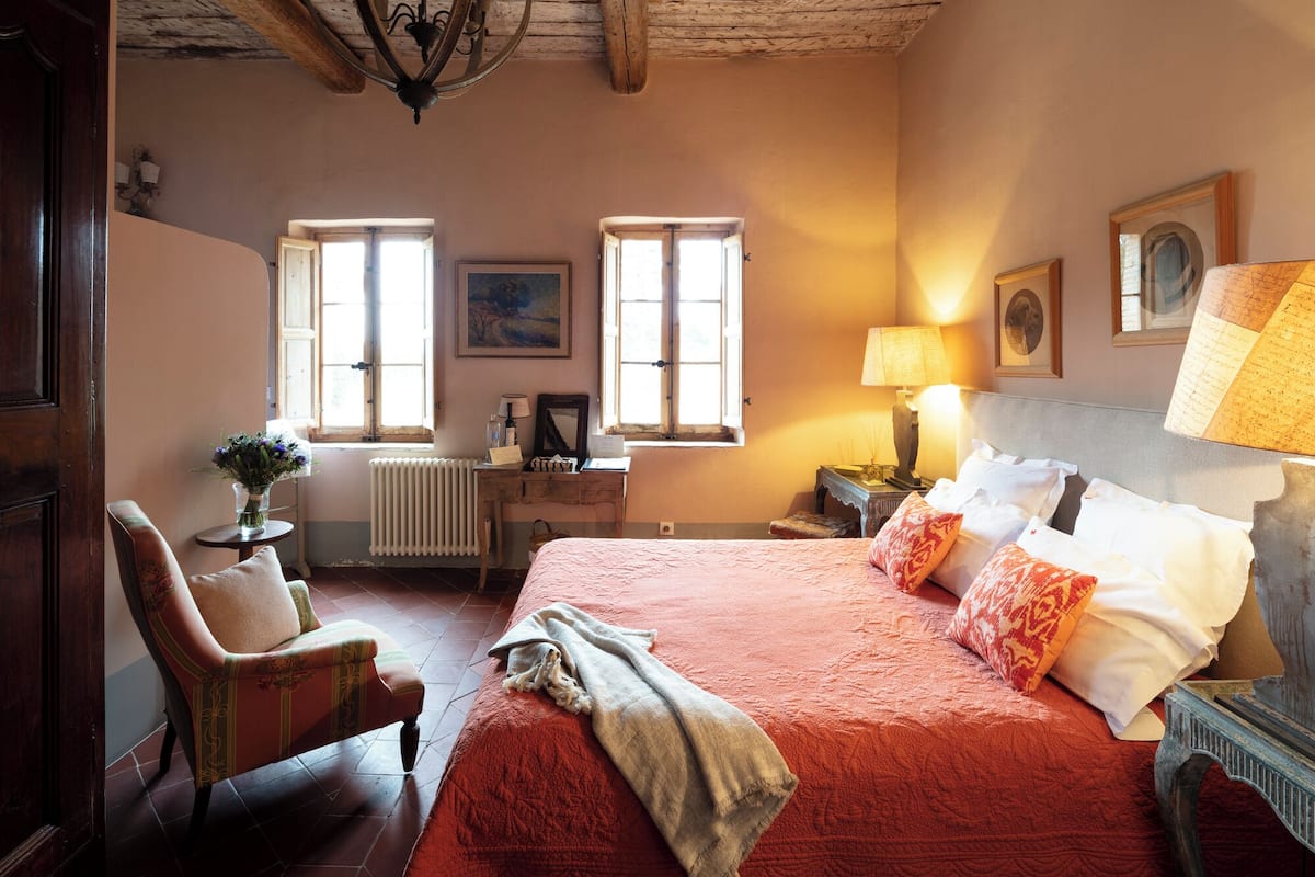 Quarto com uma cama grande, duas janelas, uma cadeira, uma mesa e um radiador.
