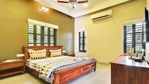 Quarto com cama de madeira, duas janelas com persianas, ventilador de teto, ar condicionado e mesa de cabeceira com abajur.