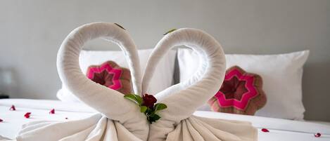 Uma cama com toalhas dispostas em formato de cisne e pétalas de rosa.
