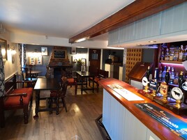 Uma área de bar com móveis de madeira, um balcão com vários tipos de bebida e um menu em lousa.