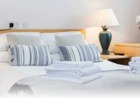 Cama bem arrumada com almofadas listradas, uma toalha branca dobrada e um abajur verde sobre uma mesa de cabeceira.